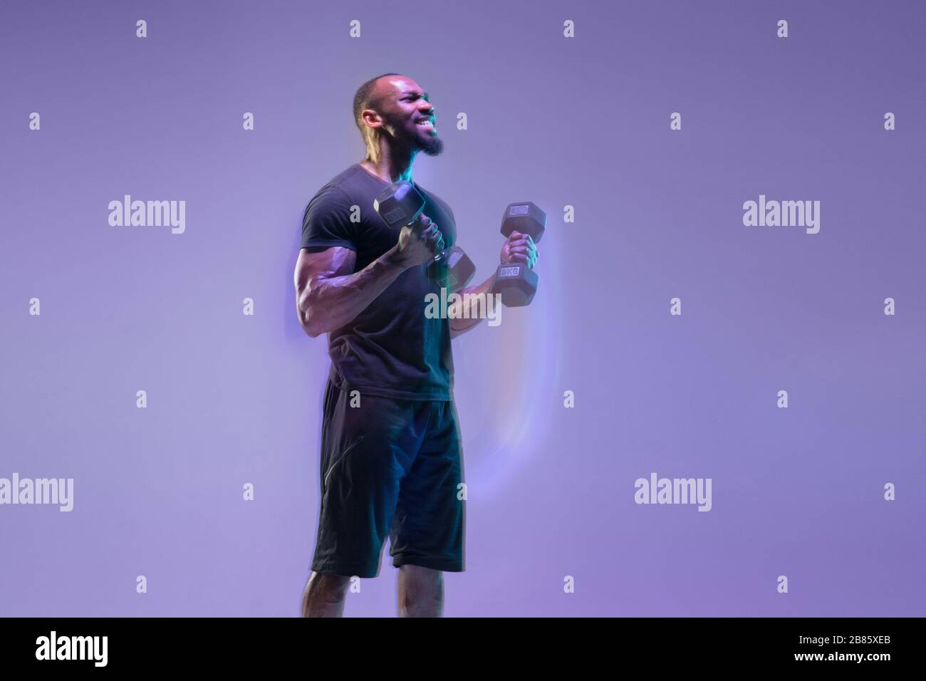 Emotions. Young african-american bodybuilder training over purple ...