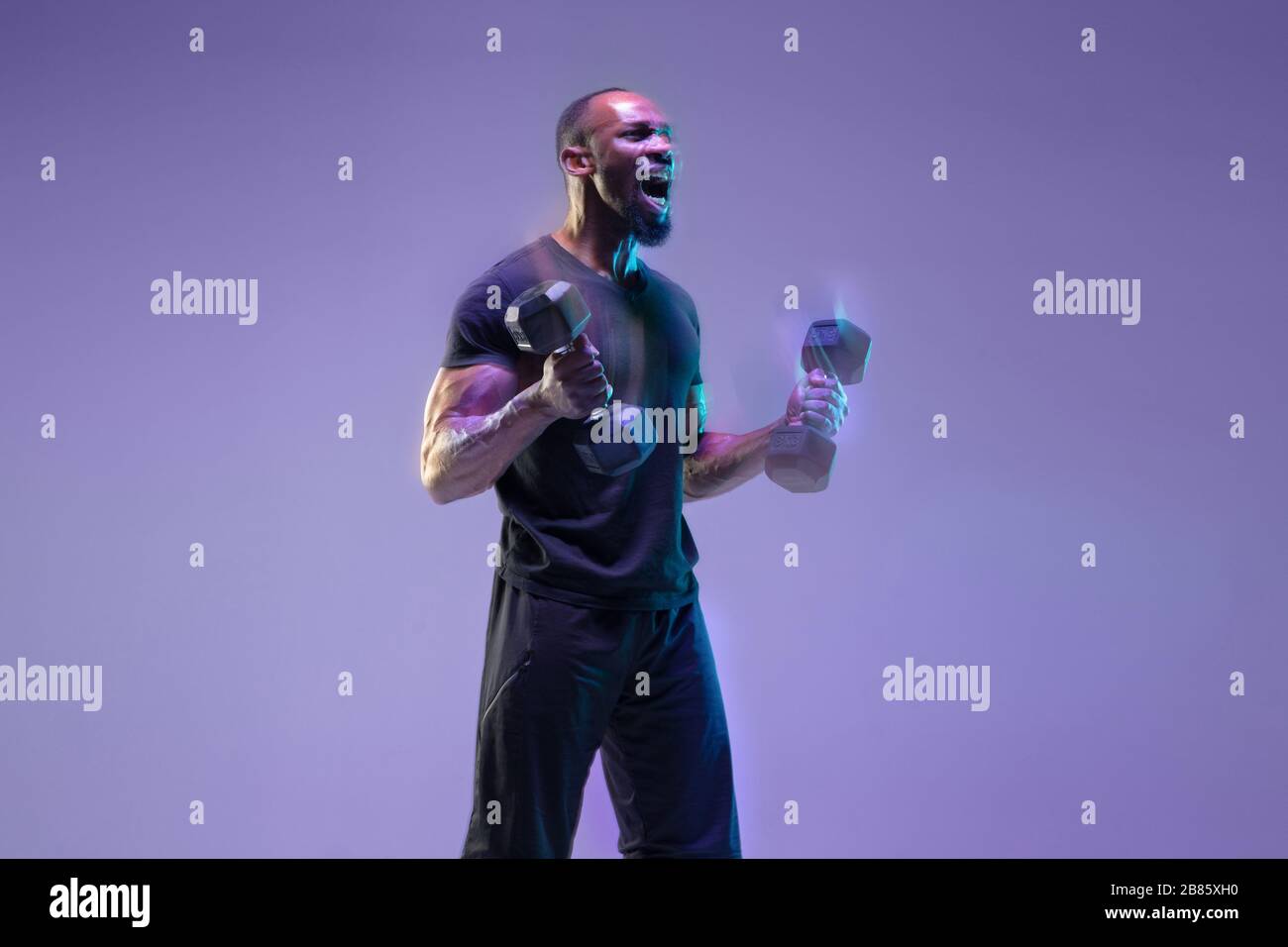 Emotions. Young african-american bodybuilder training over purple ...
