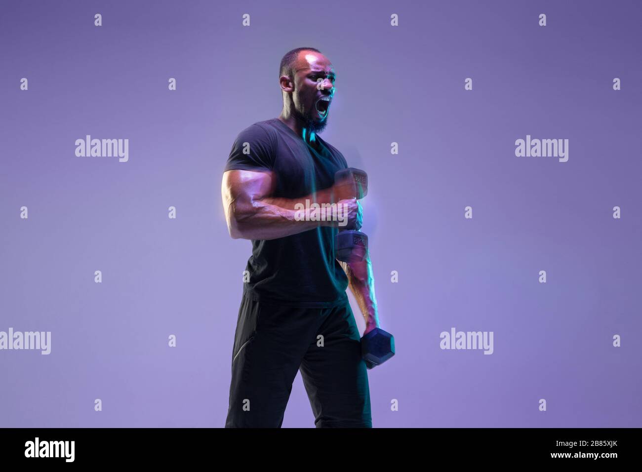 Emotional. Young african-american bodybuilder training over purple ...