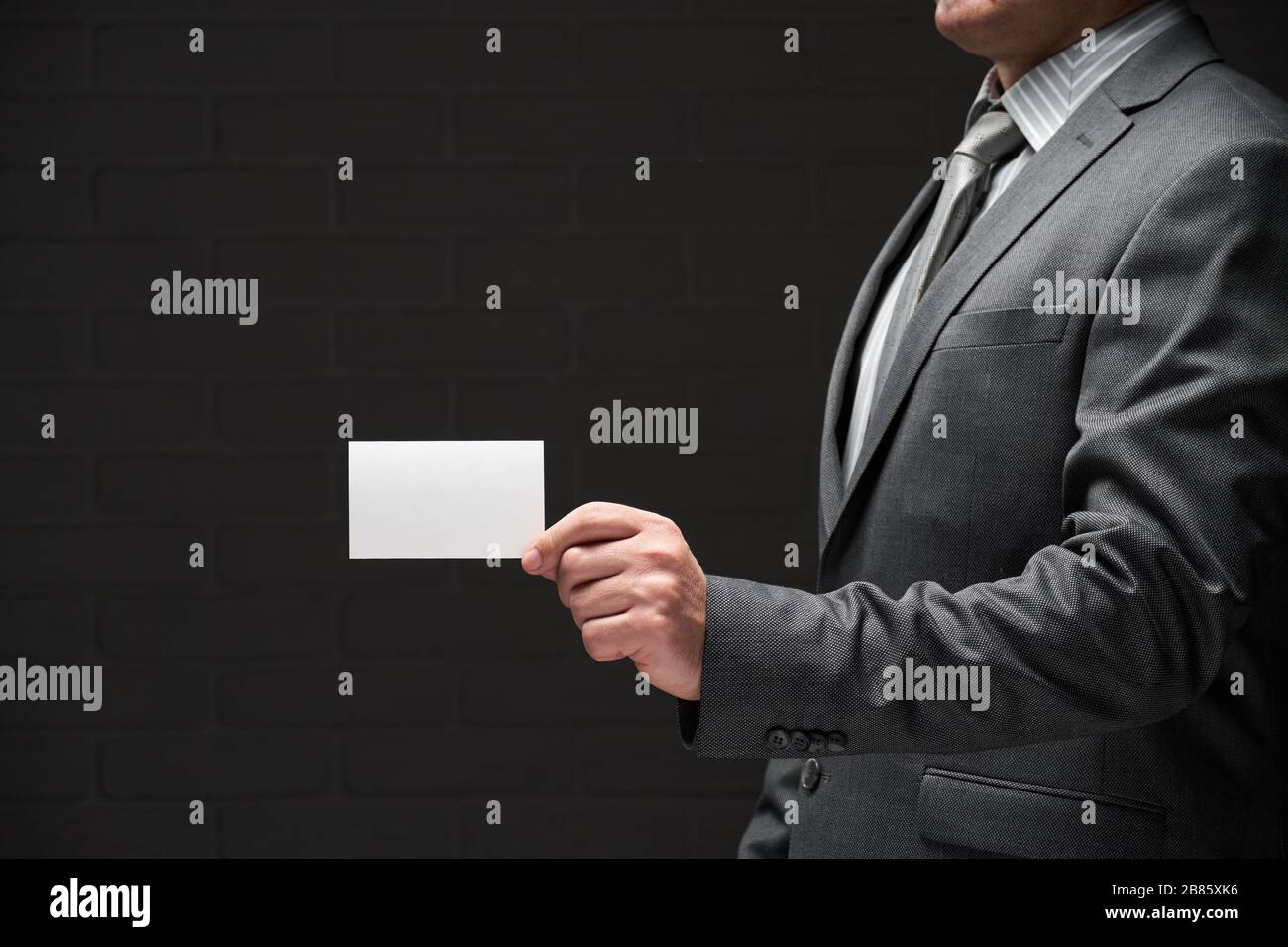 white blank business card closeup in businessman hand, gray suit, dark wall background Stock ...