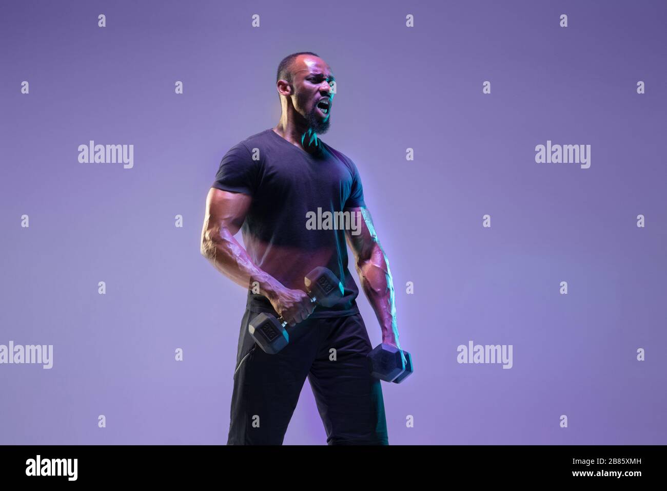 Emotional. Young african-american bodybuilder training over purple ...