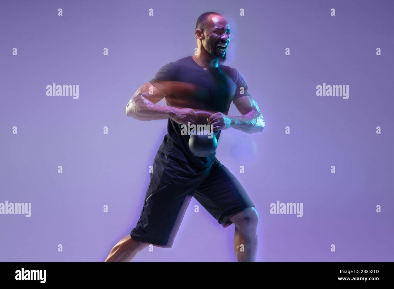 Emotional. Young african-american bodybuilder training over purple ...