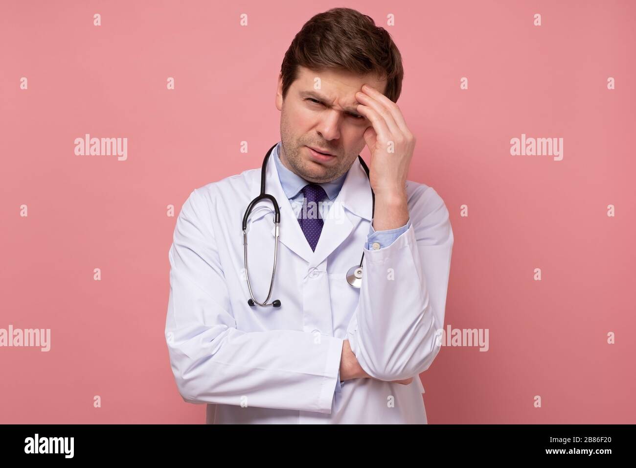 Caucasian mature doctor having headache and stress scrubs touching head ...