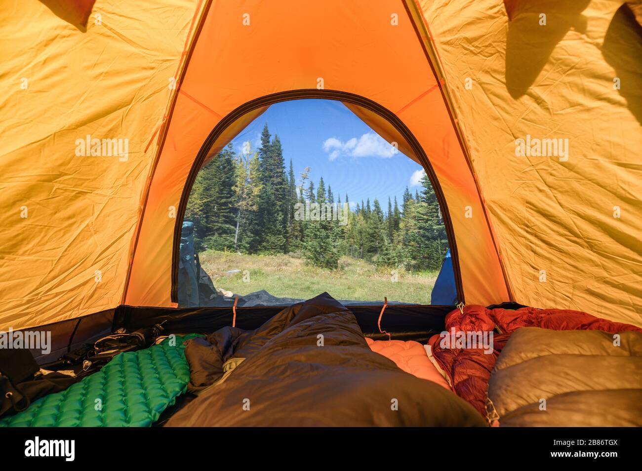 Camping with traveler stretching legs in sleeping bag on orange tent in ...