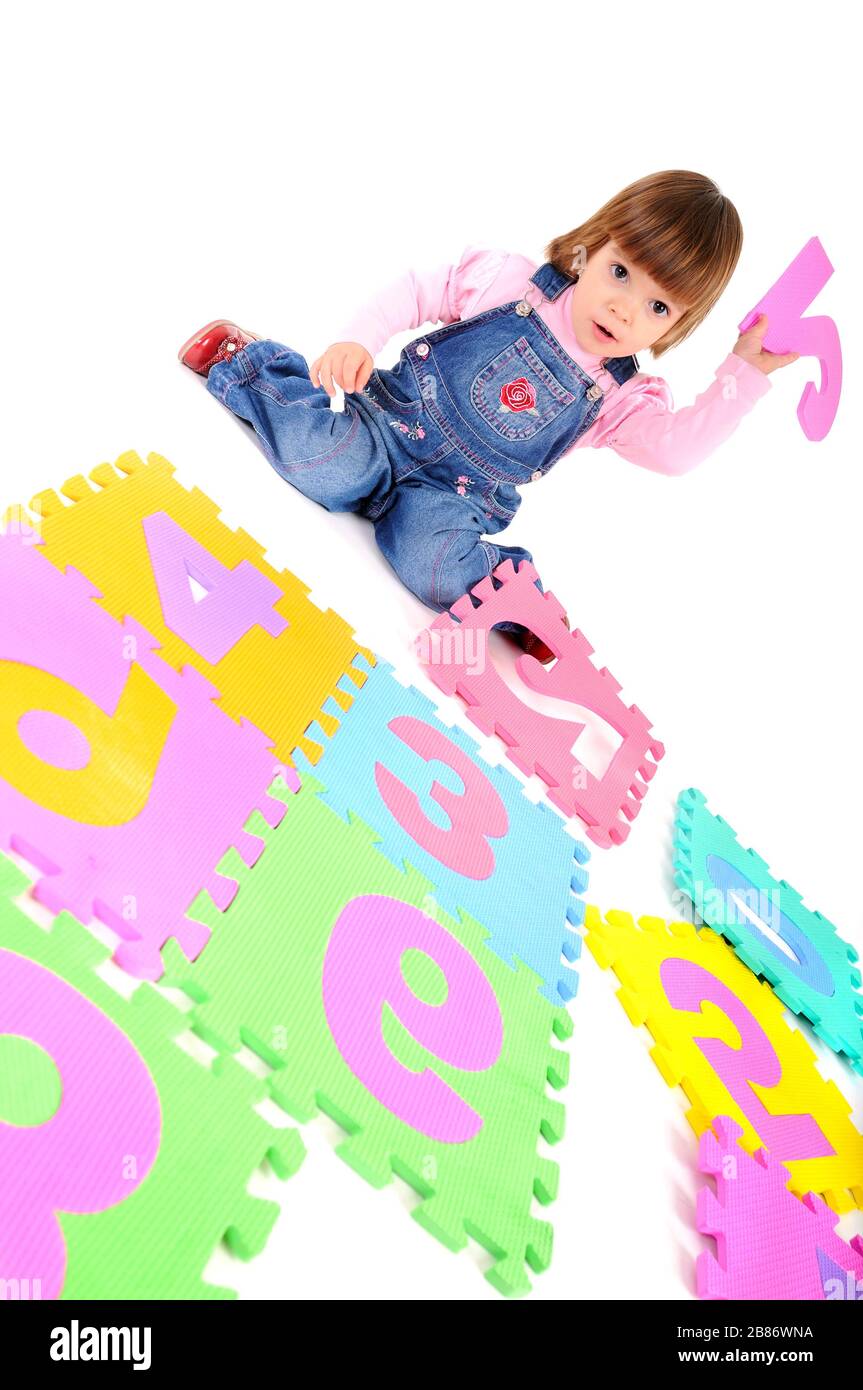 Small girl in jeans jumpsuit learning numbers and holding two in hand ...