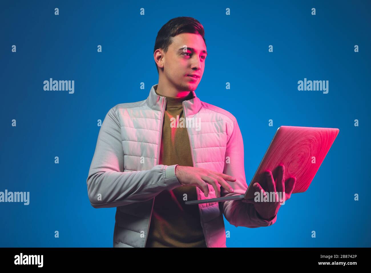 Using laptop. Caucasian man's portrait isolated on blue studio ...
