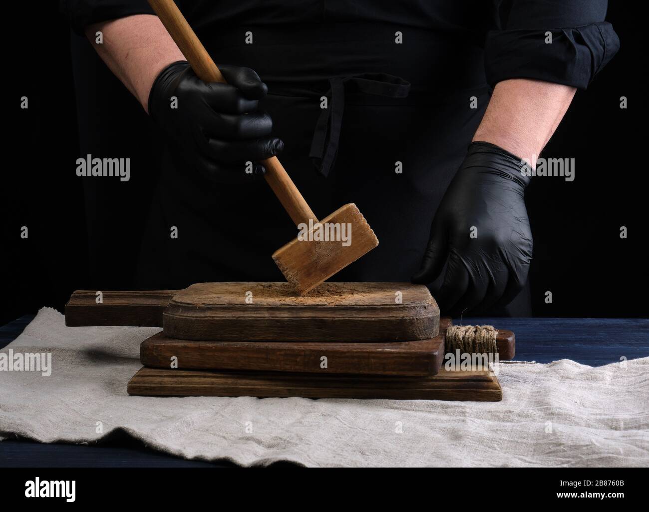 male cook in black uniform holds a wooden hammer for beating meat on a ...