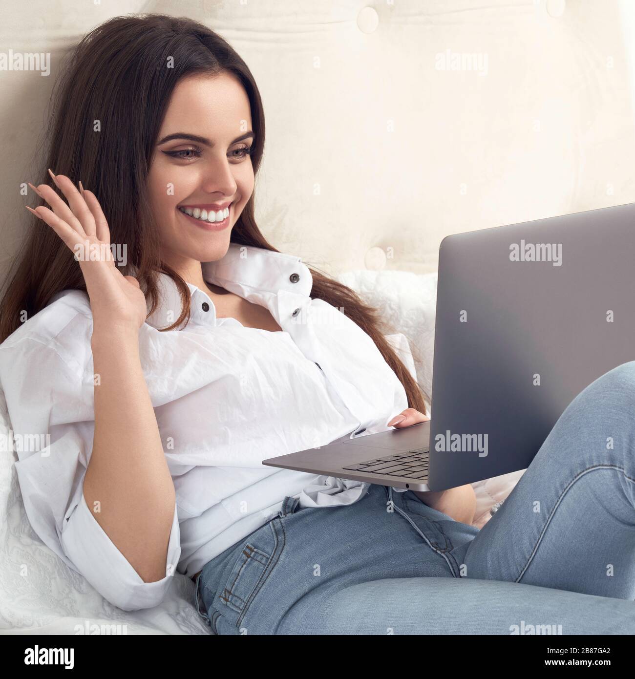 Pretty girl waving hand to video call on laptop and laying in bed Stock ...