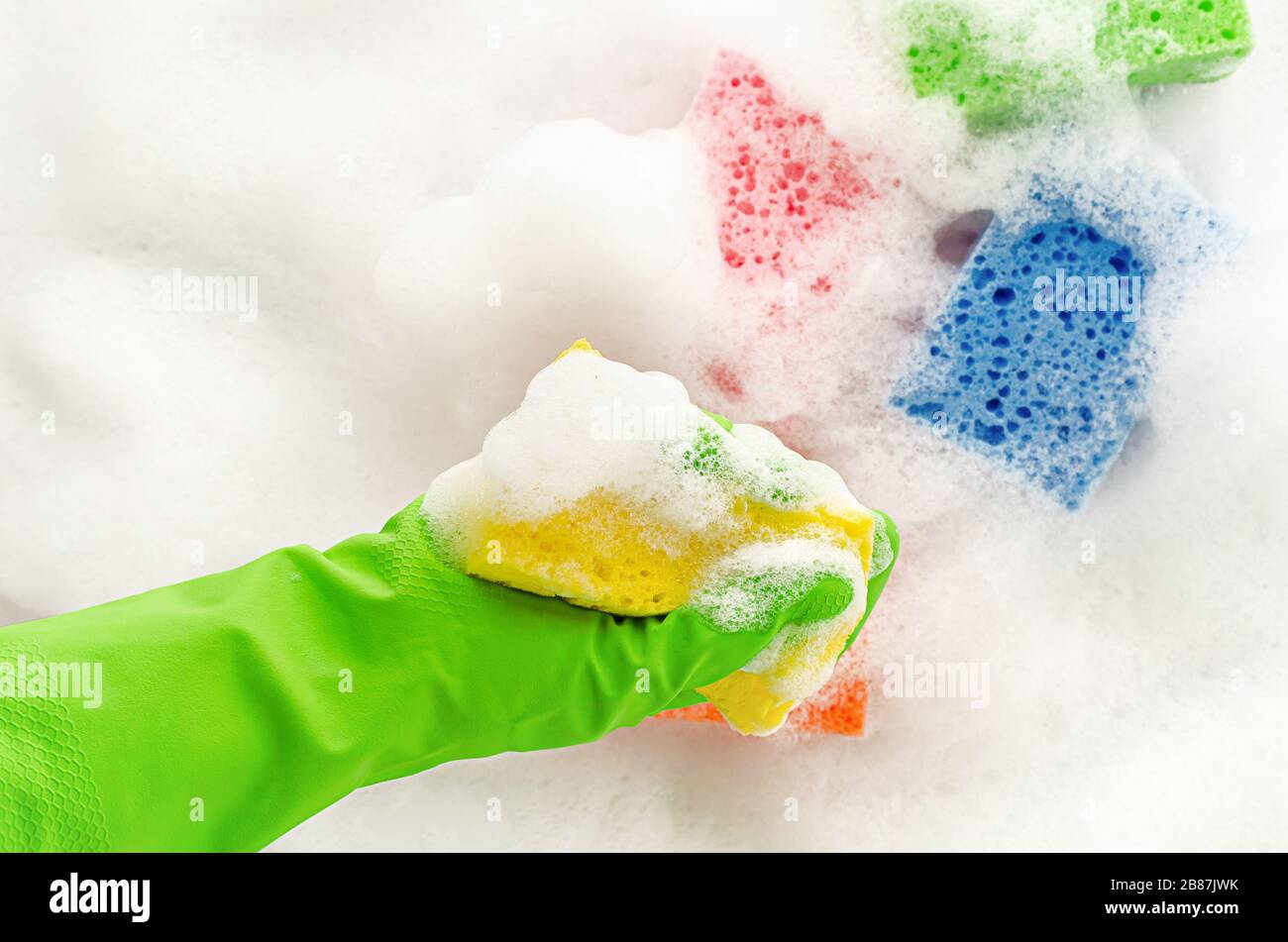 Hand in protective glove holding a soapy sponge on foam background ...