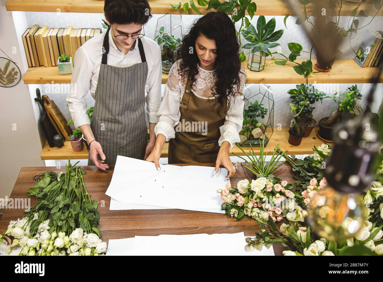 An attractive, experienced female florist teaches a young man how to ...