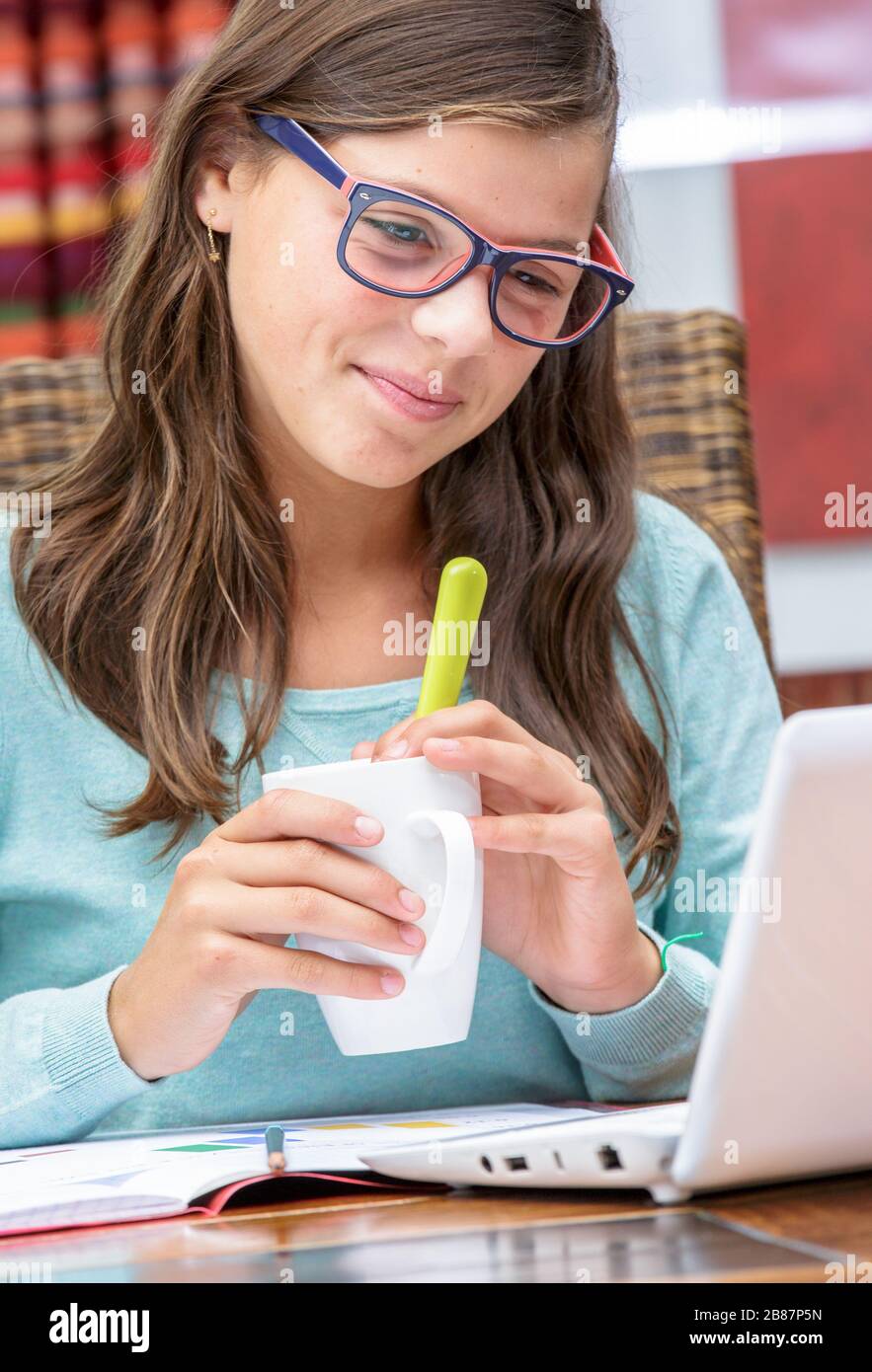 pretty student girl doing homework at home with a laptop and drinking ...