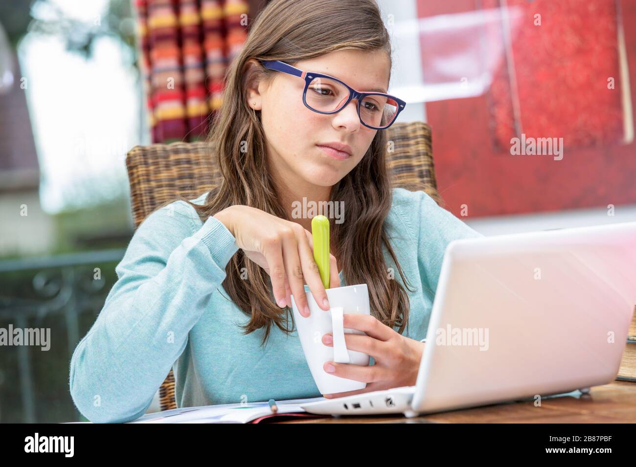 pretty student girl doing homework at home with a laptop and drinking ...
