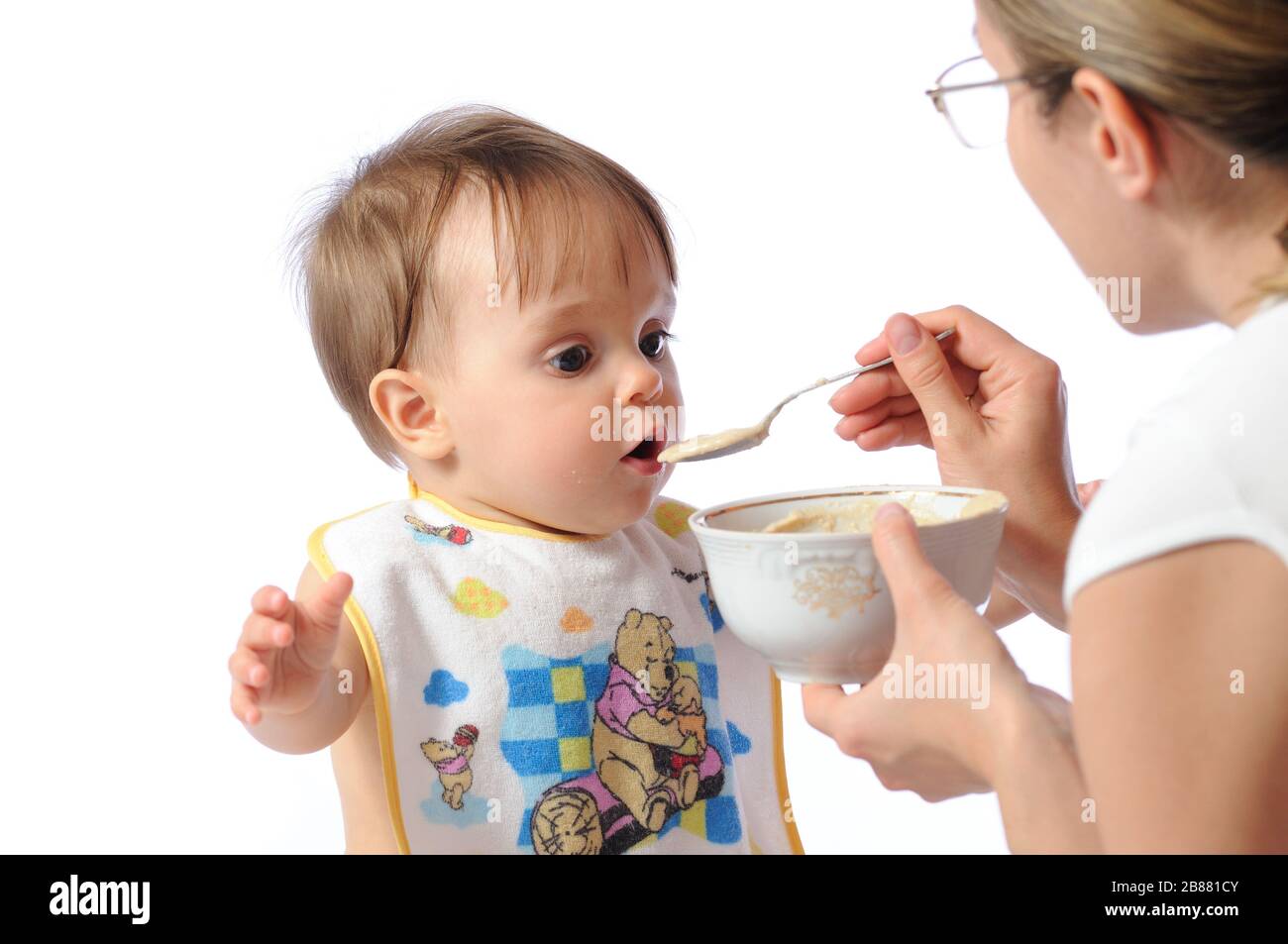 Surprised cute little baby girl eating food from spoon. Mother holding ...