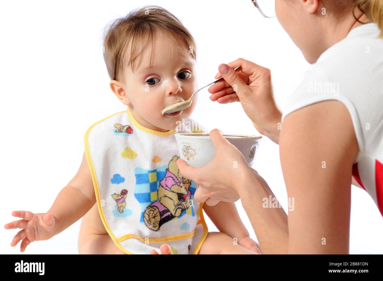 Surprised cute little baby girl eating food from spoon. Mother holding ...