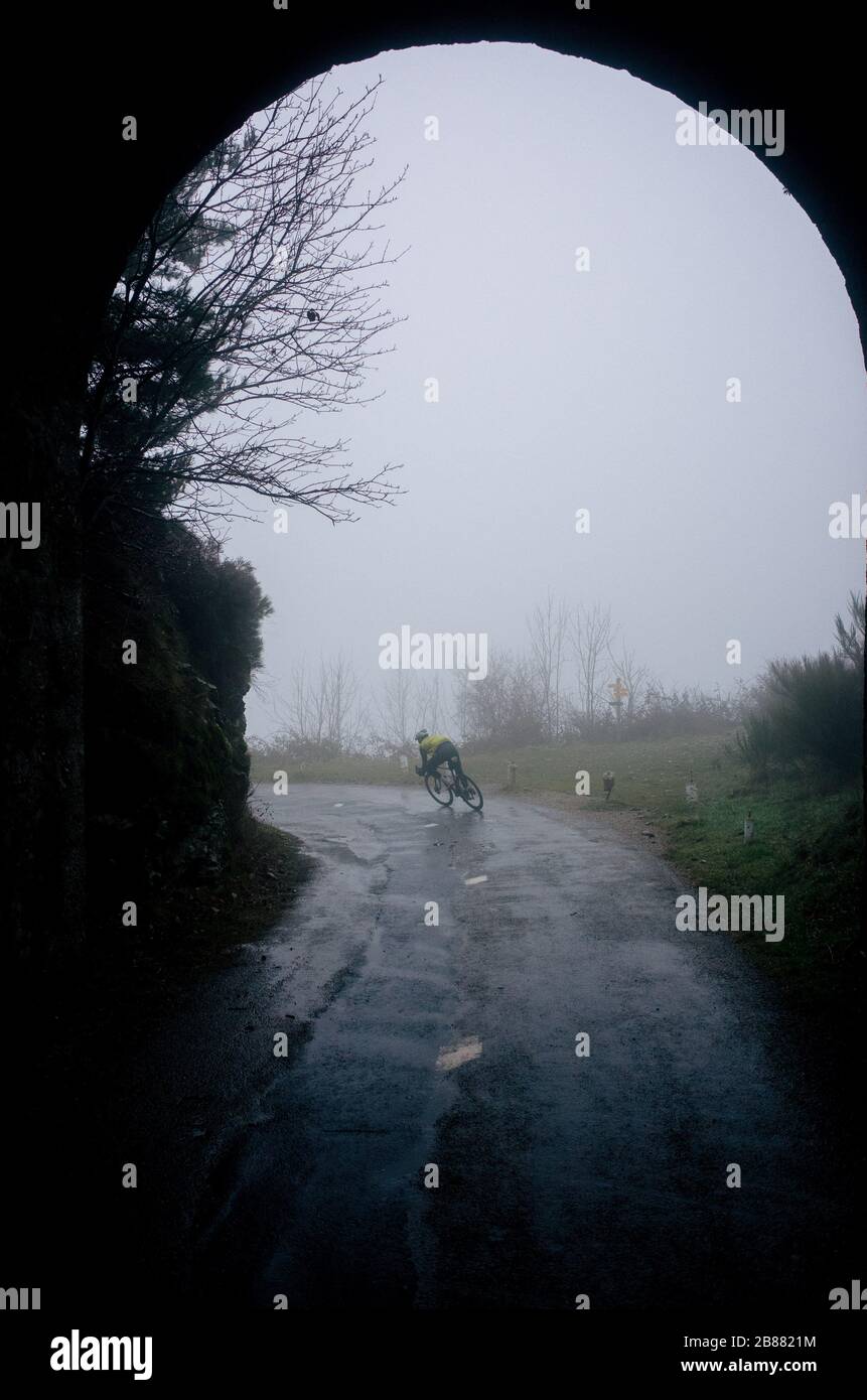 Male cyclist descends fast in windy rainy and cold corner at summit of ...