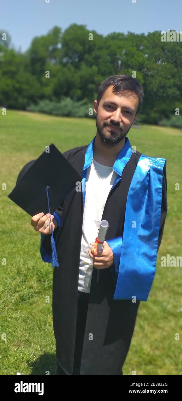 Young Graduate Person Holds His Diploma and Graduation Cap in a Grassy ...