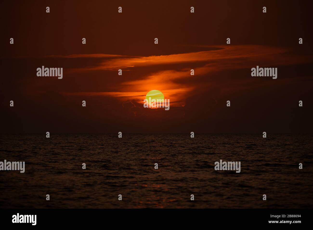 Orange and red sunset over the sea with clouds surrounding the sun and ...