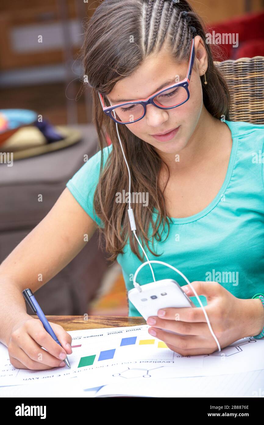 pretty student doing homework while listening to music on her phone ...