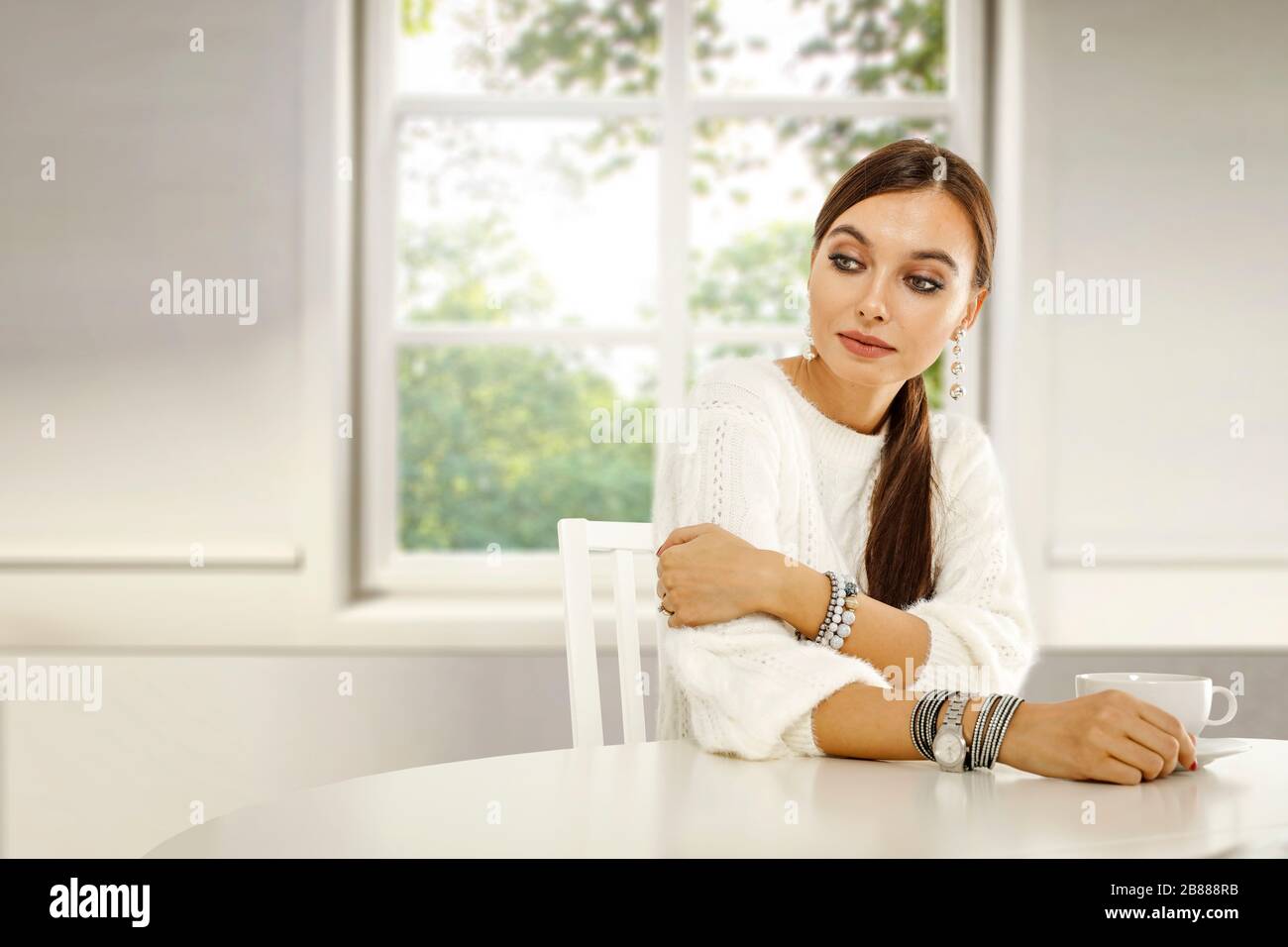 Slim young woman sitting in kitchen with white wooden table.Empty place ...