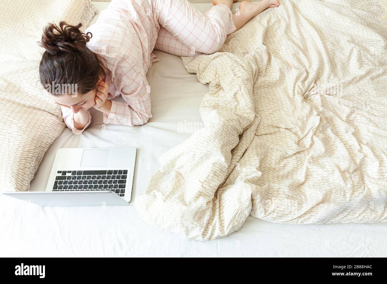 Mobile Office at home. Young woman in pajamas sitting on bed at home ...