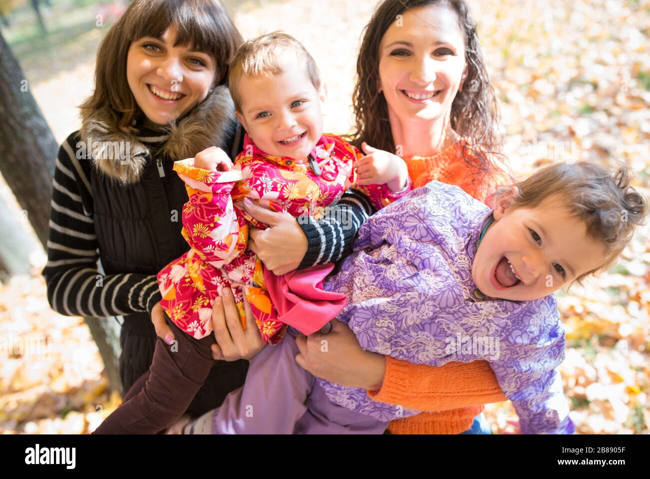Young smiling mom friends and their little and cute children are walking outside in the park on ...
