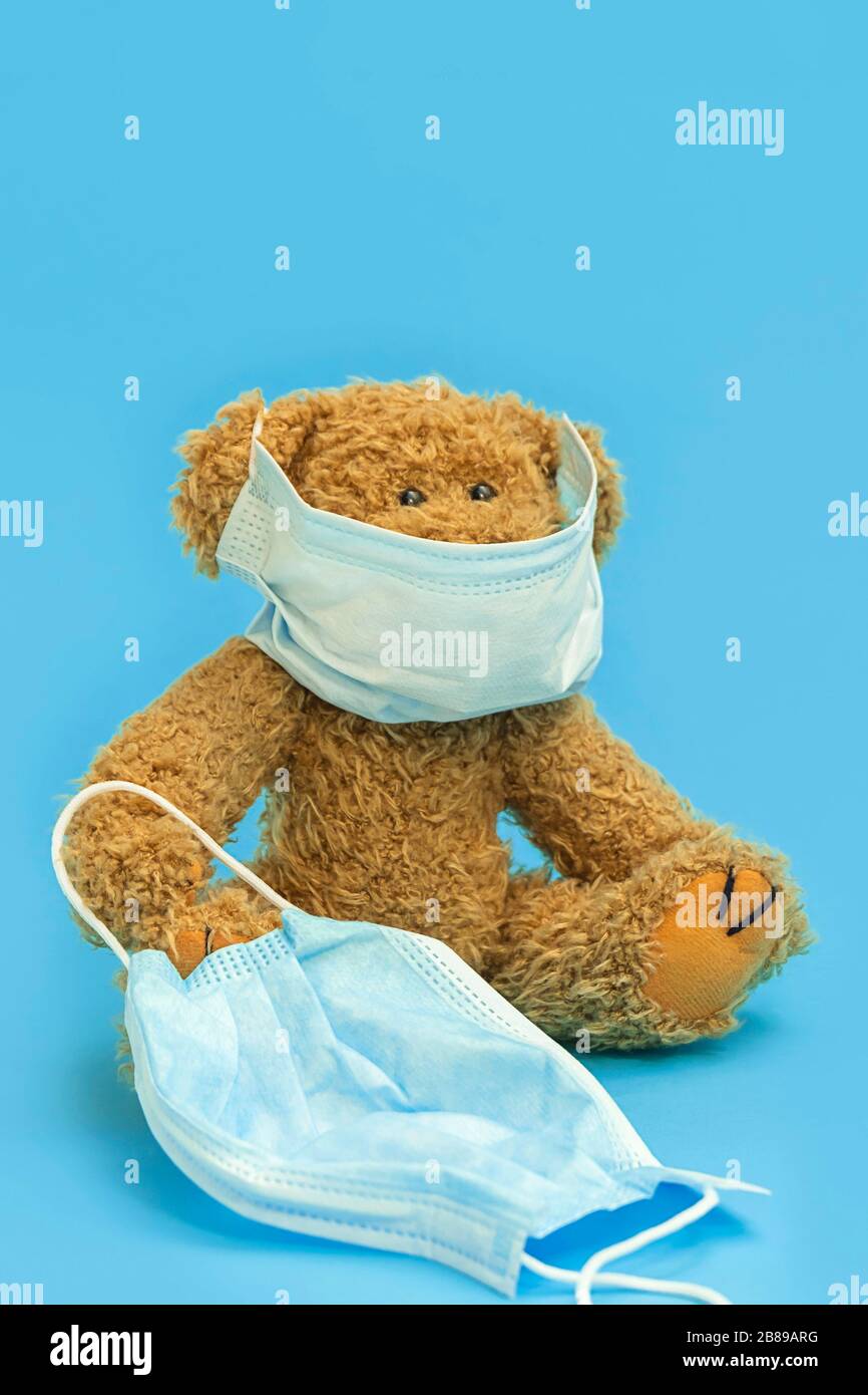 Brown teddy bear wearing face mask and holding one mask in his arm on ...