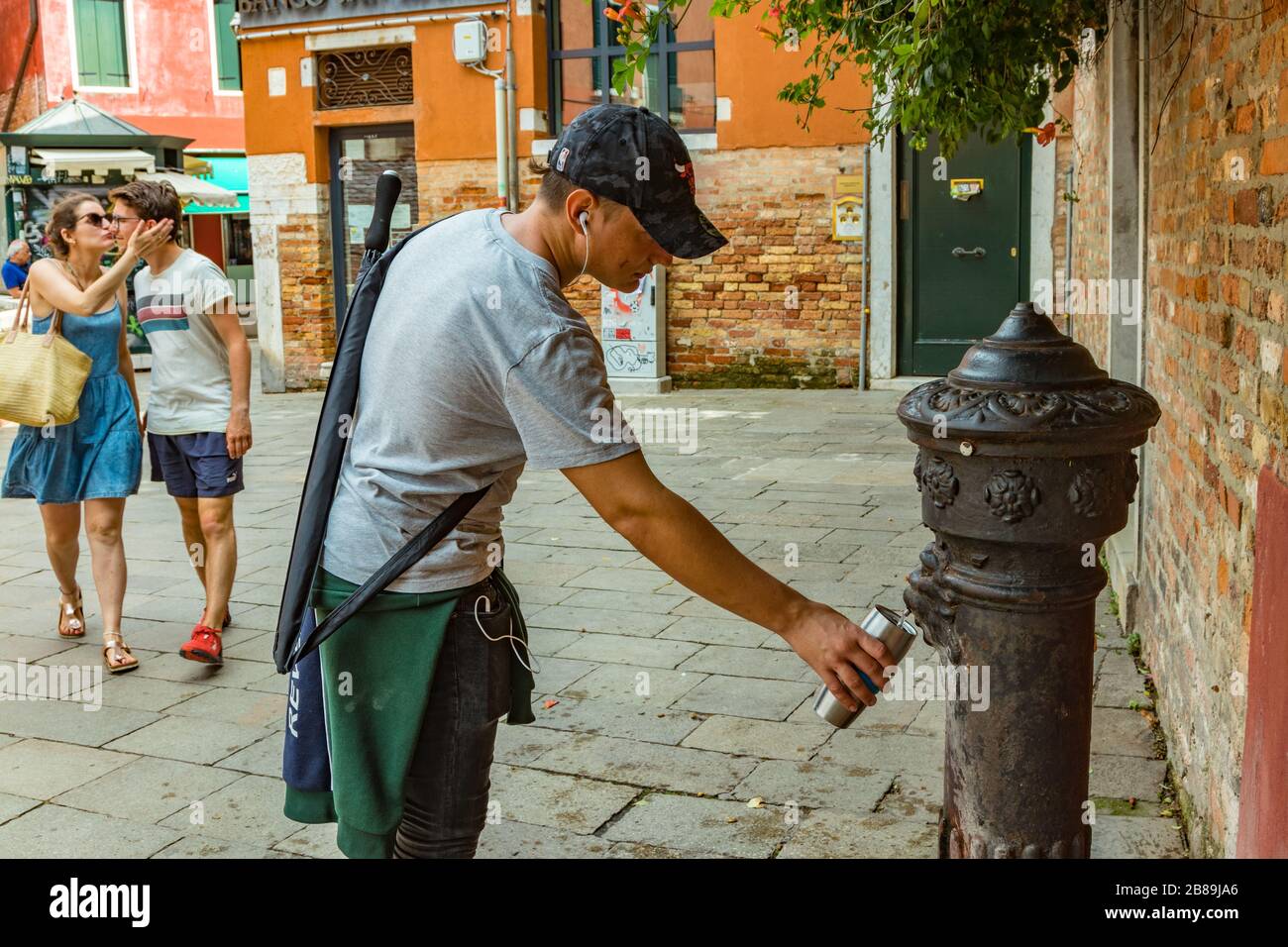 Man filling metal flask thermos using Old bronze public street tap for ...