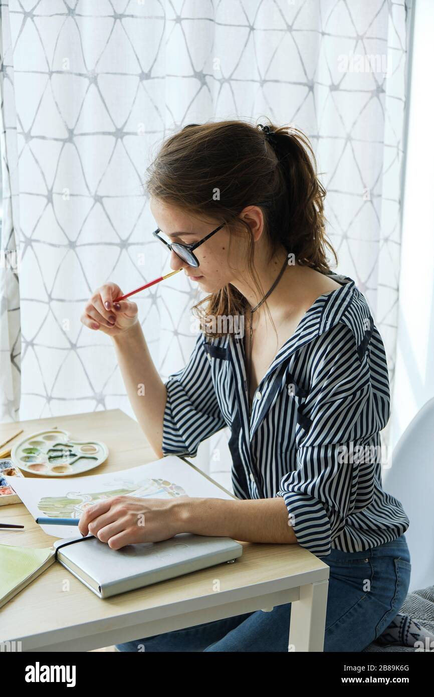 millennial girl draws fabulous images on paper while sitting at home ...