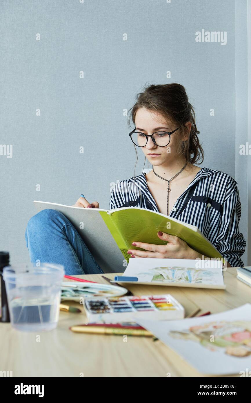 millennial girl draws fabulous images on paper while sitting at home ...