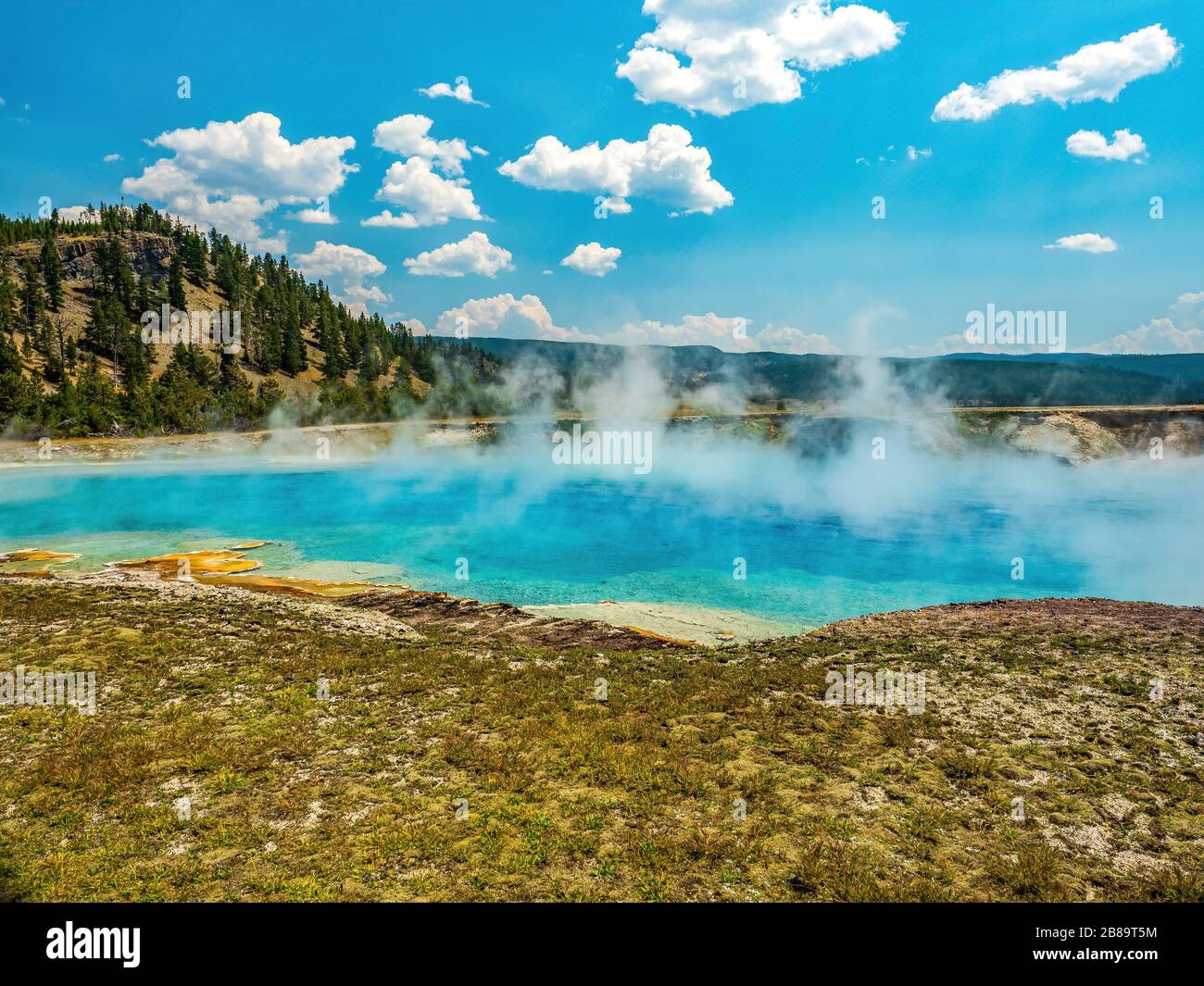 blue hot springs in Yellowstone National Park on a sunny day with mist ...