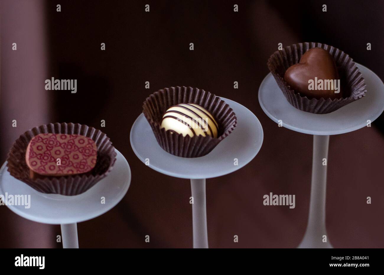 A variety of fancy chocolates are displayed on glass pedestals at a ...