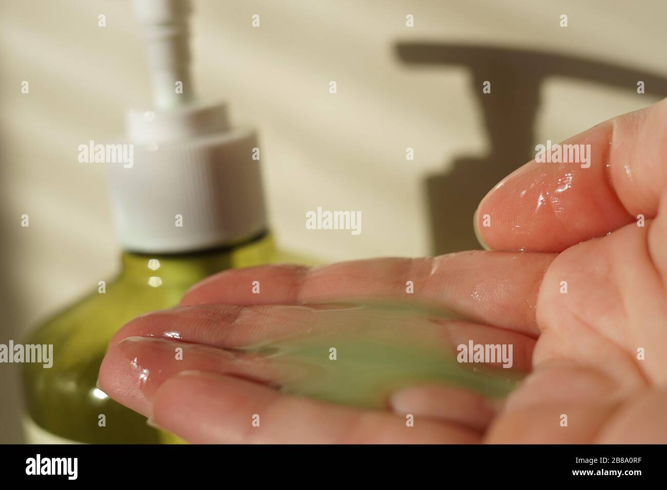 A female hand uses liquid soap with a dispenser. Green drop of gel in ...