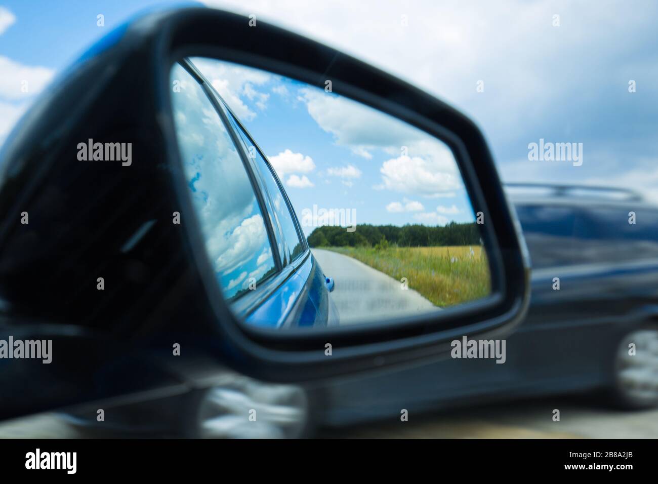 Side rear-view mirror car reflection of a winding road in a forest or ...