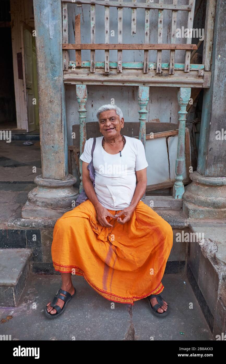 A Hindu priest clad in an orange dhoti relaxes outside his residence at ...