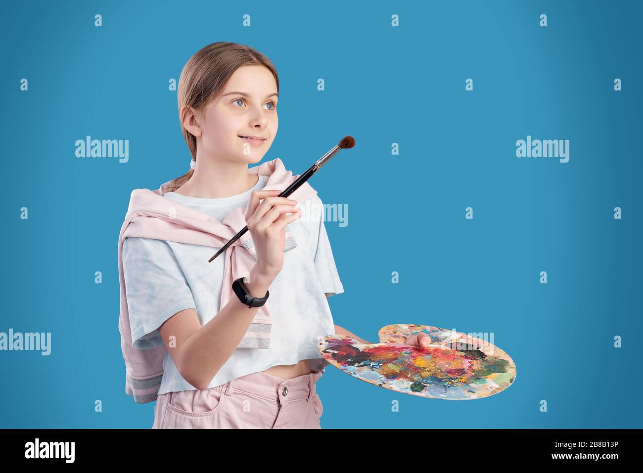 Pretty teenage student in t-shirt and jeans holding paintbrush and ...
