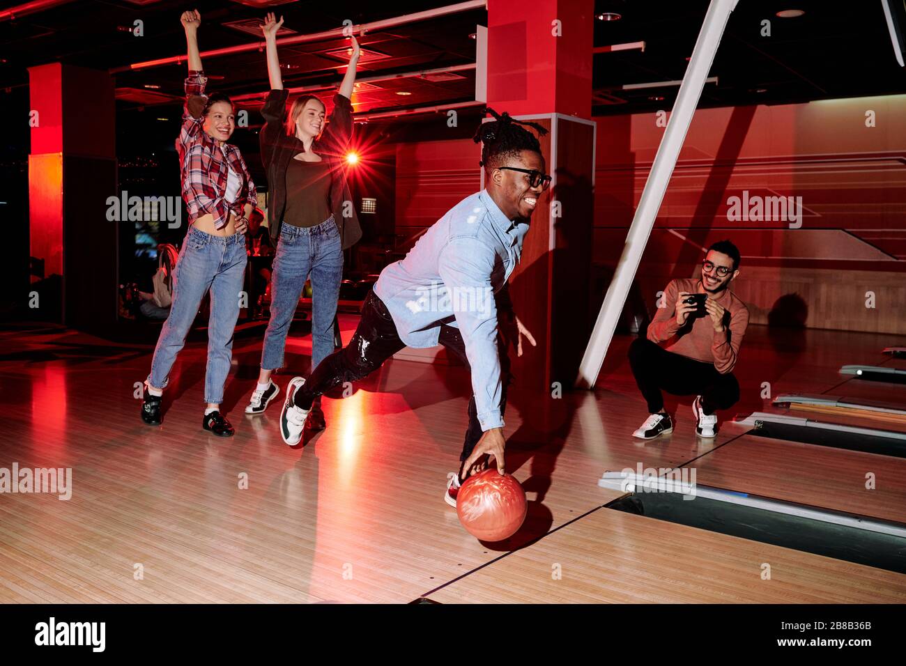 Cheerful active guy of African ethnicity going to throw bowling ball ...