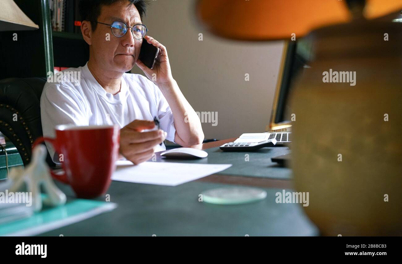 Man working from home, on his cell phone and facing computer screen ...