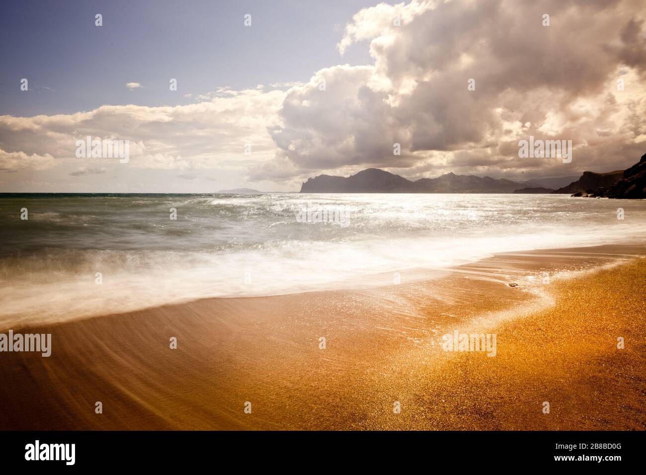 Sandy beach with mountains on background. Mountains are covered with ...