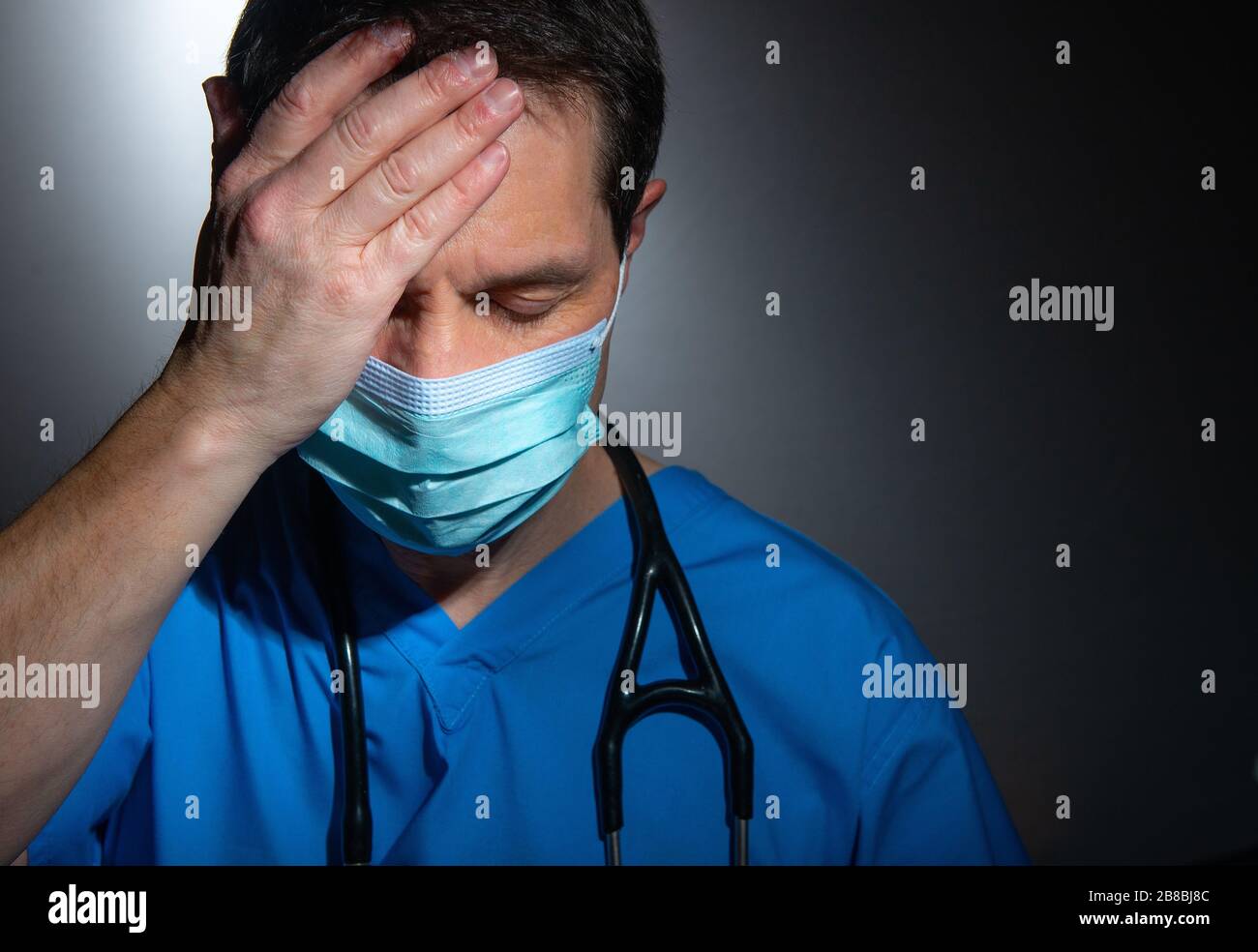Tired / exhausted doctor with hand on head and eyes closed, wearing ...