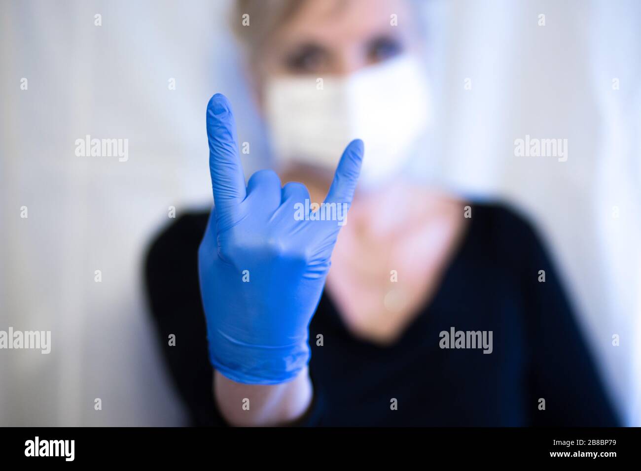 Senior woman wearing mask and wearing gloves shows the rock sign ...