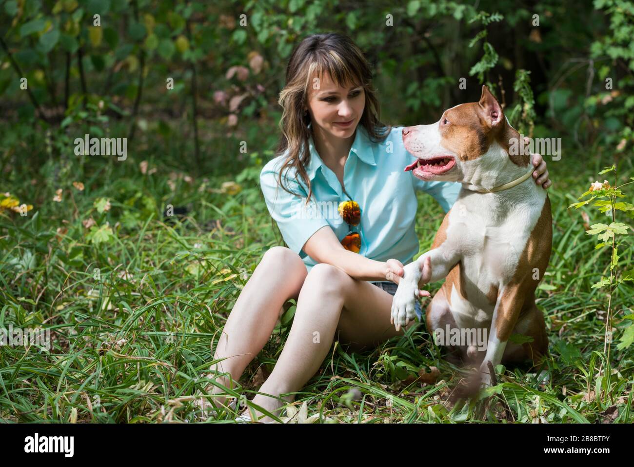 Front view of charming lady resting on grass and holding dog paw. Cute ...