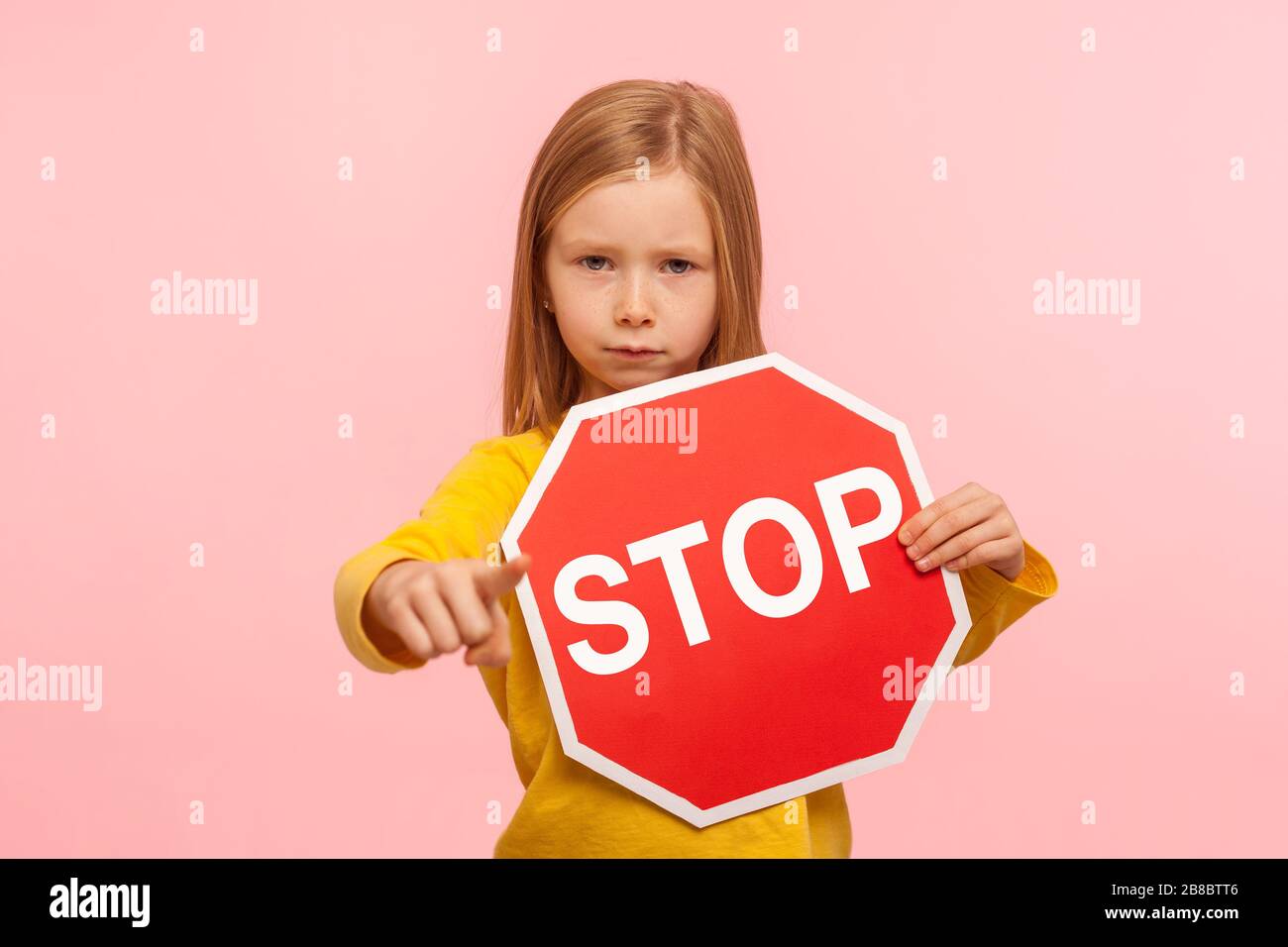 Portrait of cute serious bossy little girl holding Stop symbol, showing ...