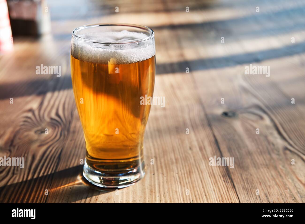 Glass of cold beer on the wooden table of a pub under natural afternoon ...