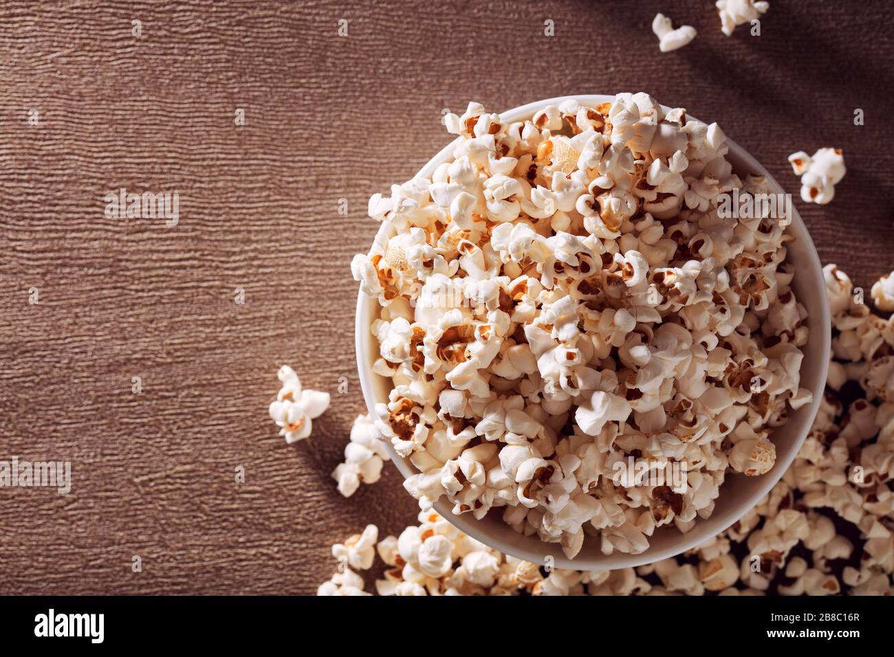 White bowl filled with popcorn spilled over the table. Watching tv ...