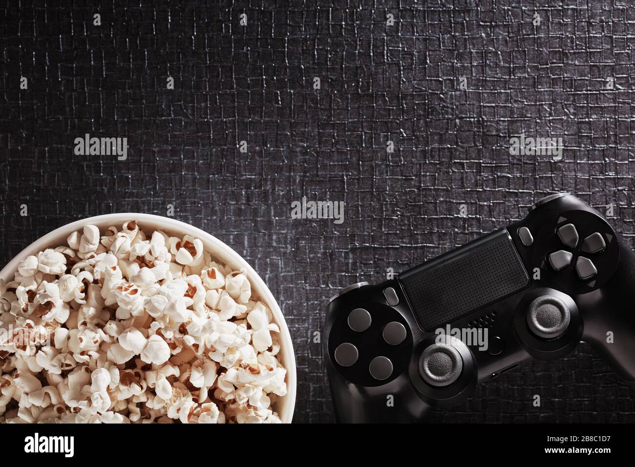 Bowl of popcorn with a gamepad on a textured black background. Play ...