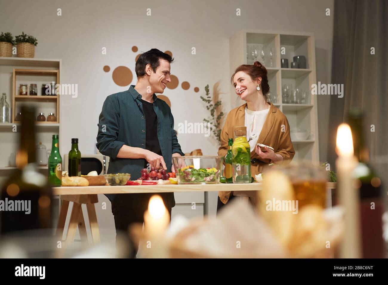 Young couple smiling to each other while cooking dinner together in ...