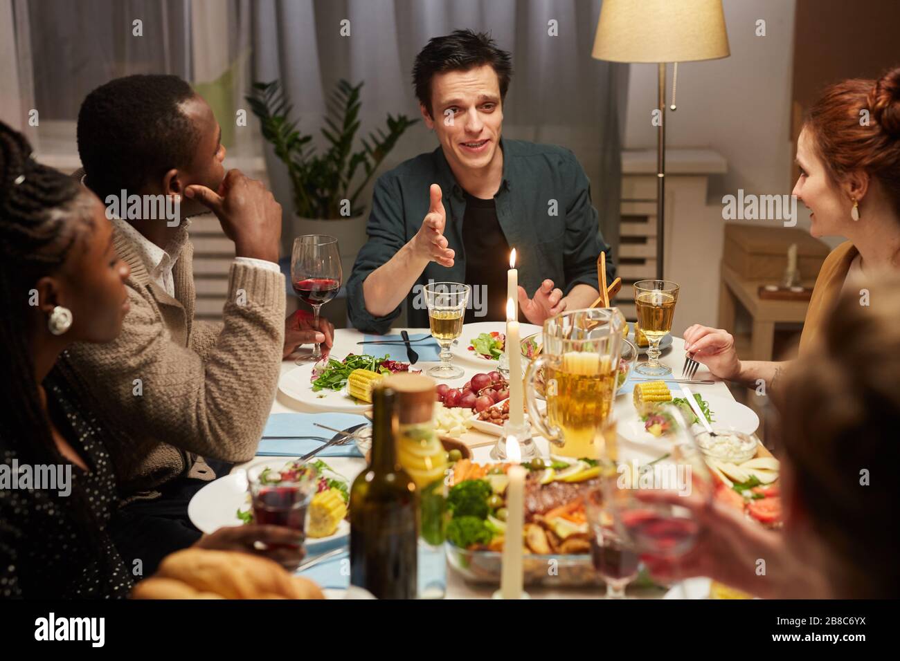 Group of friends sitting at the table and listening to young man who ...