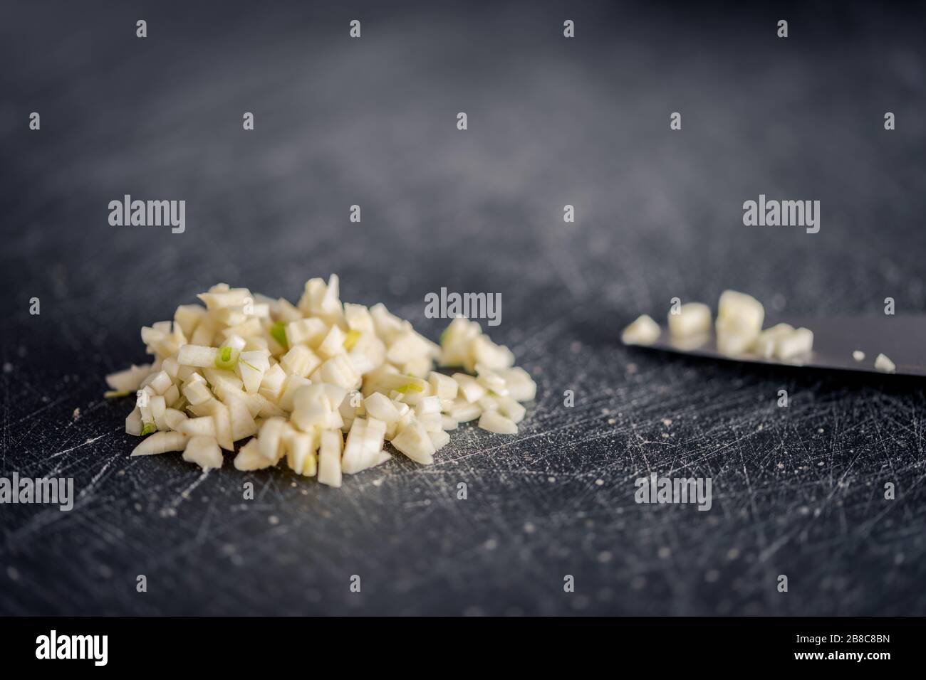Detail of small cut garlic with tip of knife lying on black kitchen ...