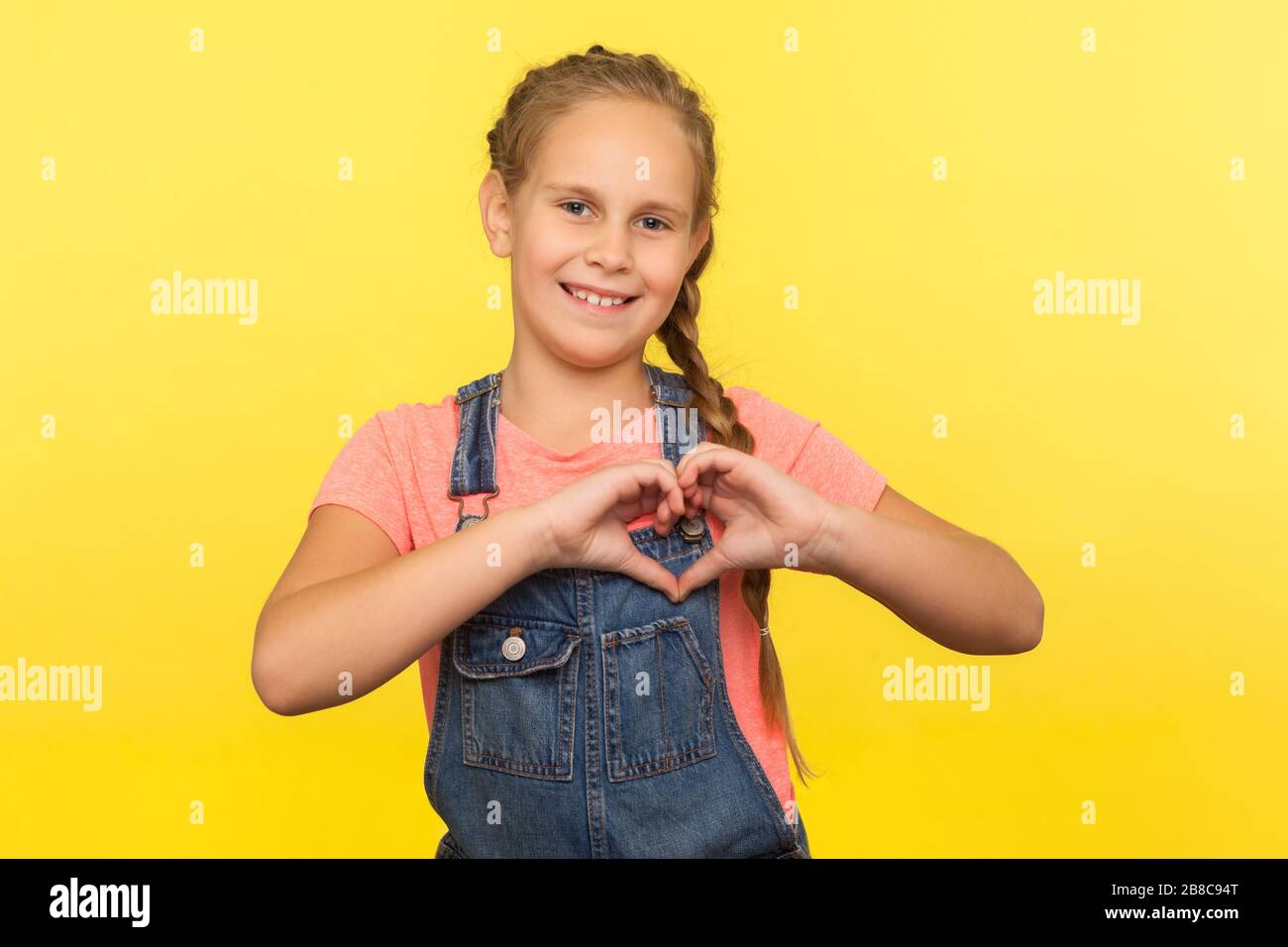 Portrait of adorable little girl with braid in denim overalls showing ...