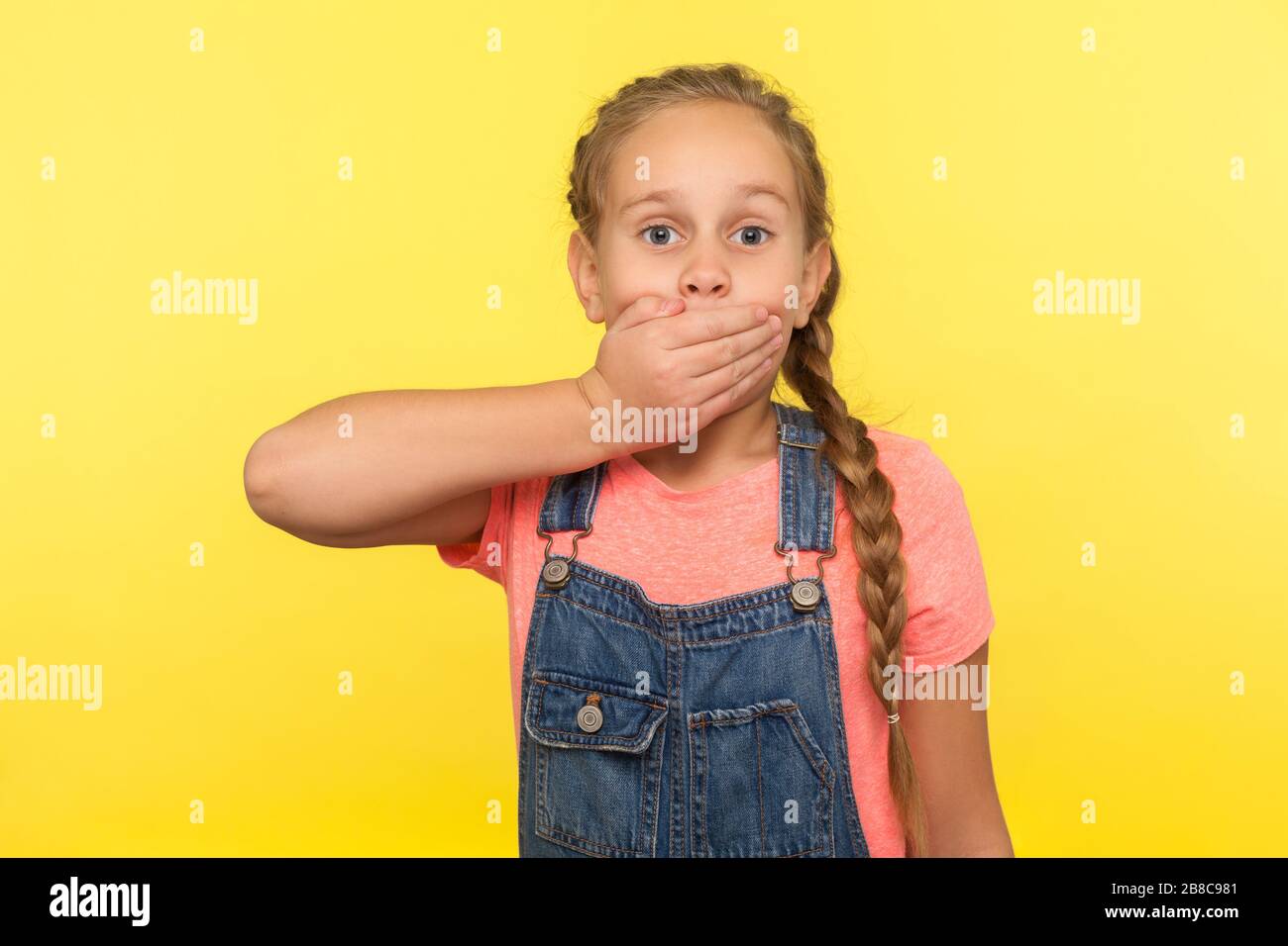 I won't tell! Portrait of scared little girl with braid in denim ...